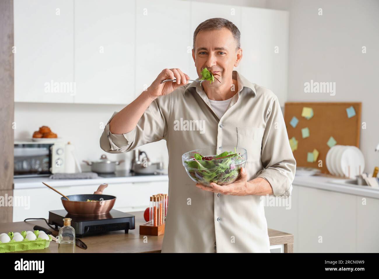 Mature man eating vegetable salad in kitchen Stock Photo - Alamy
