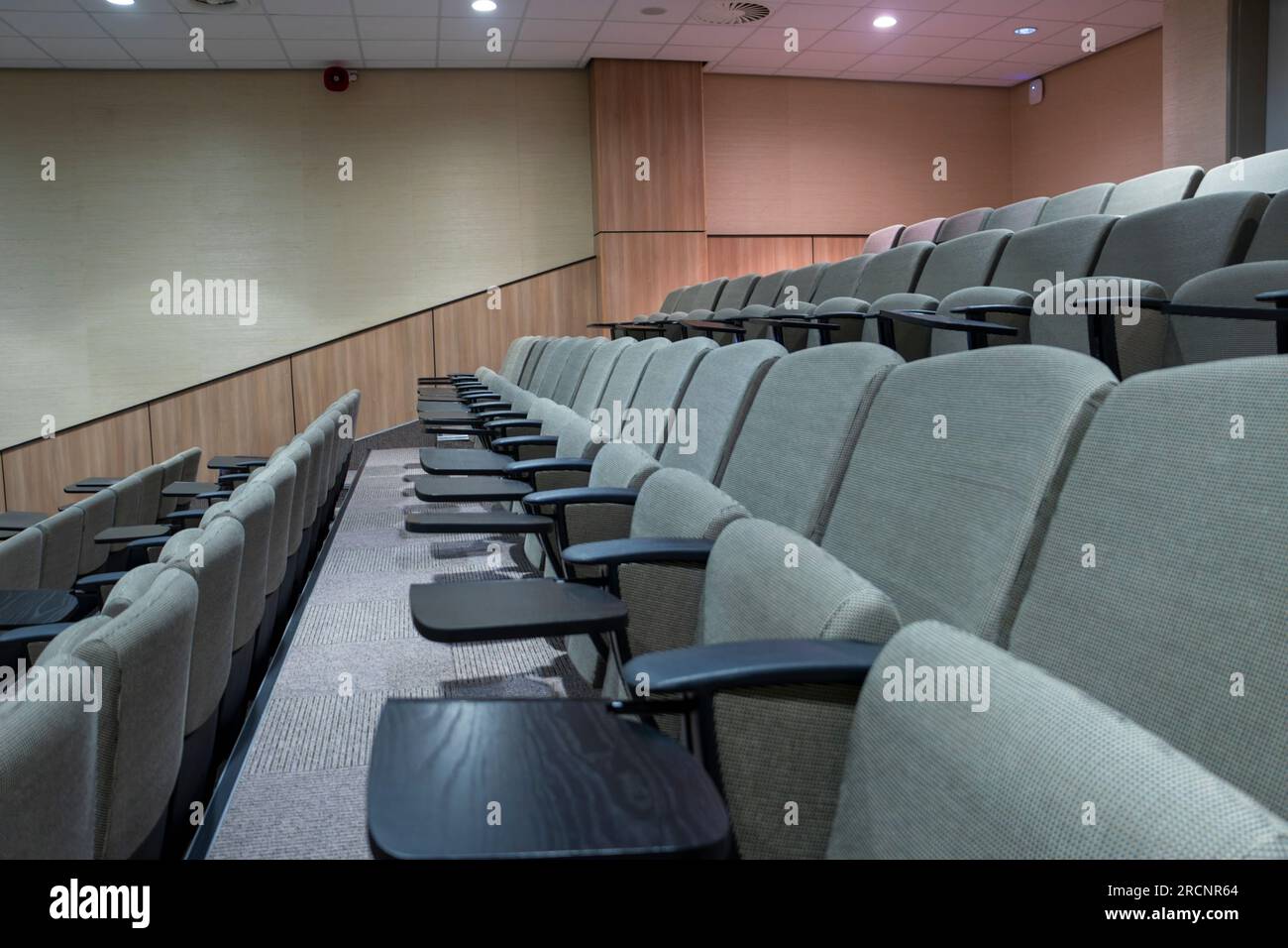 large auditorium rows of empty chairs with small side tables in a ...