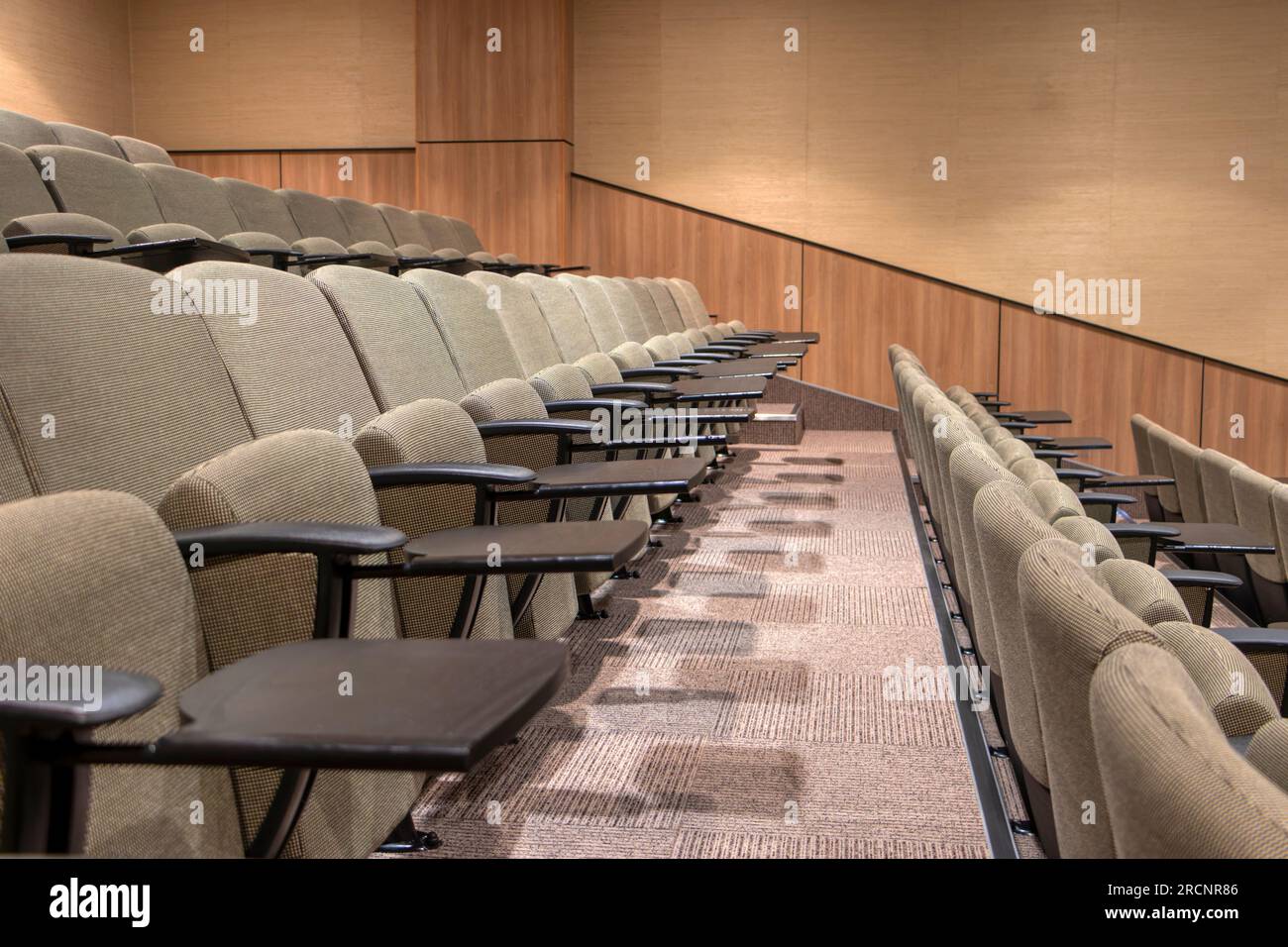 large auditorium rows of empty chairs with small side tables in a ...