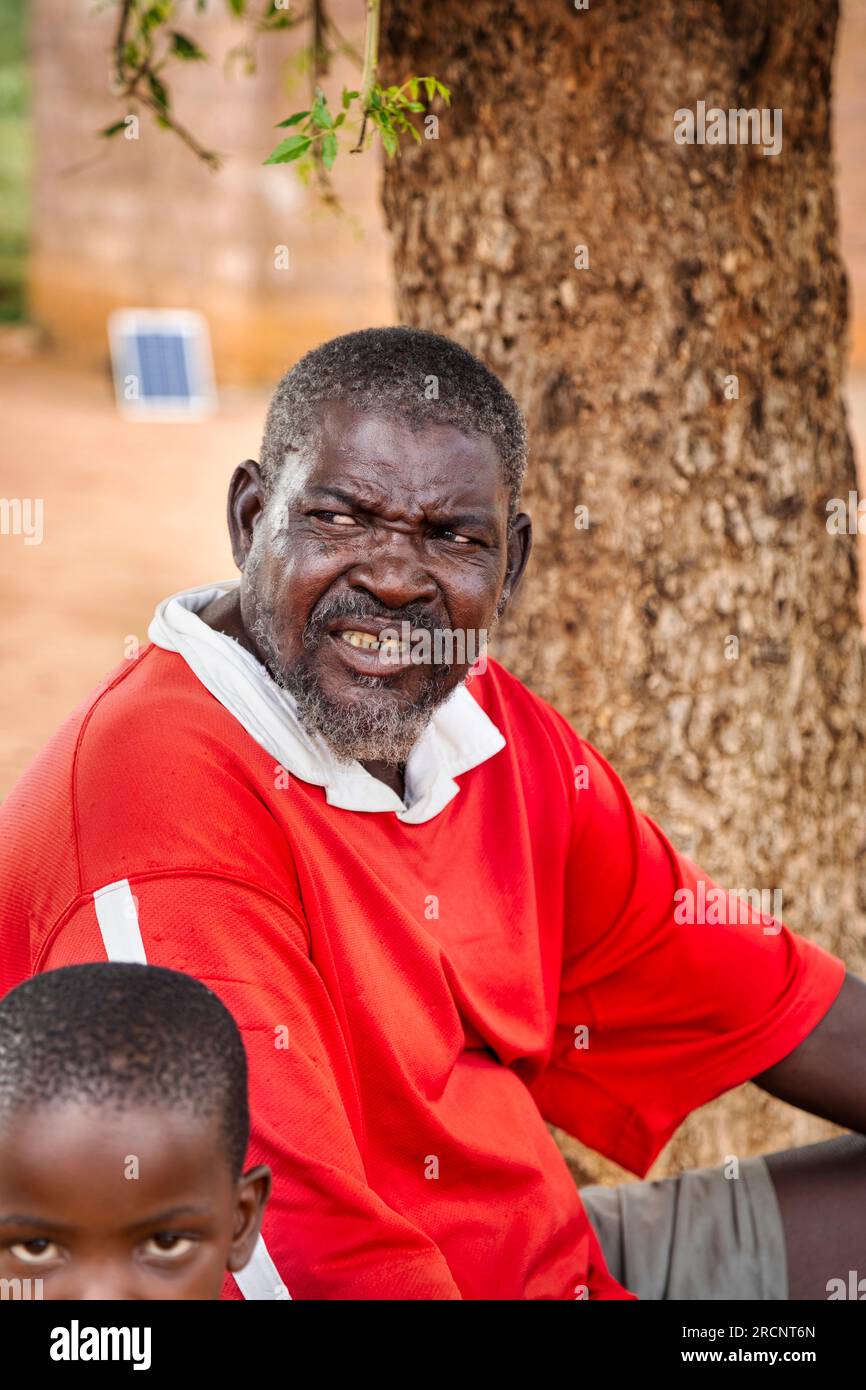 portrait of old man with red shirt and african girl in the yard ...