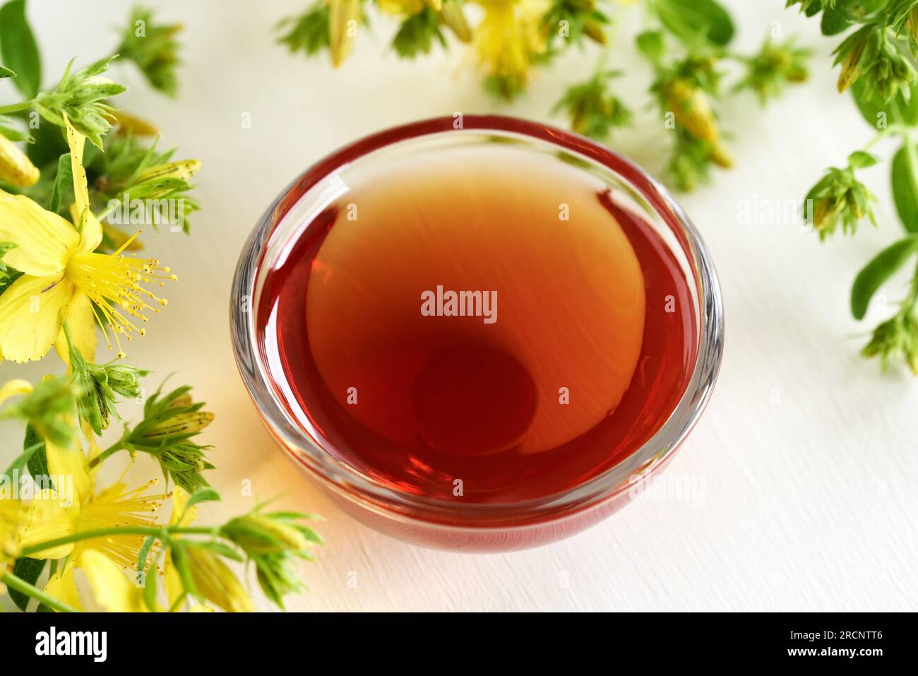 A bowl of red oil made from St. John's wort flowers on white background ...