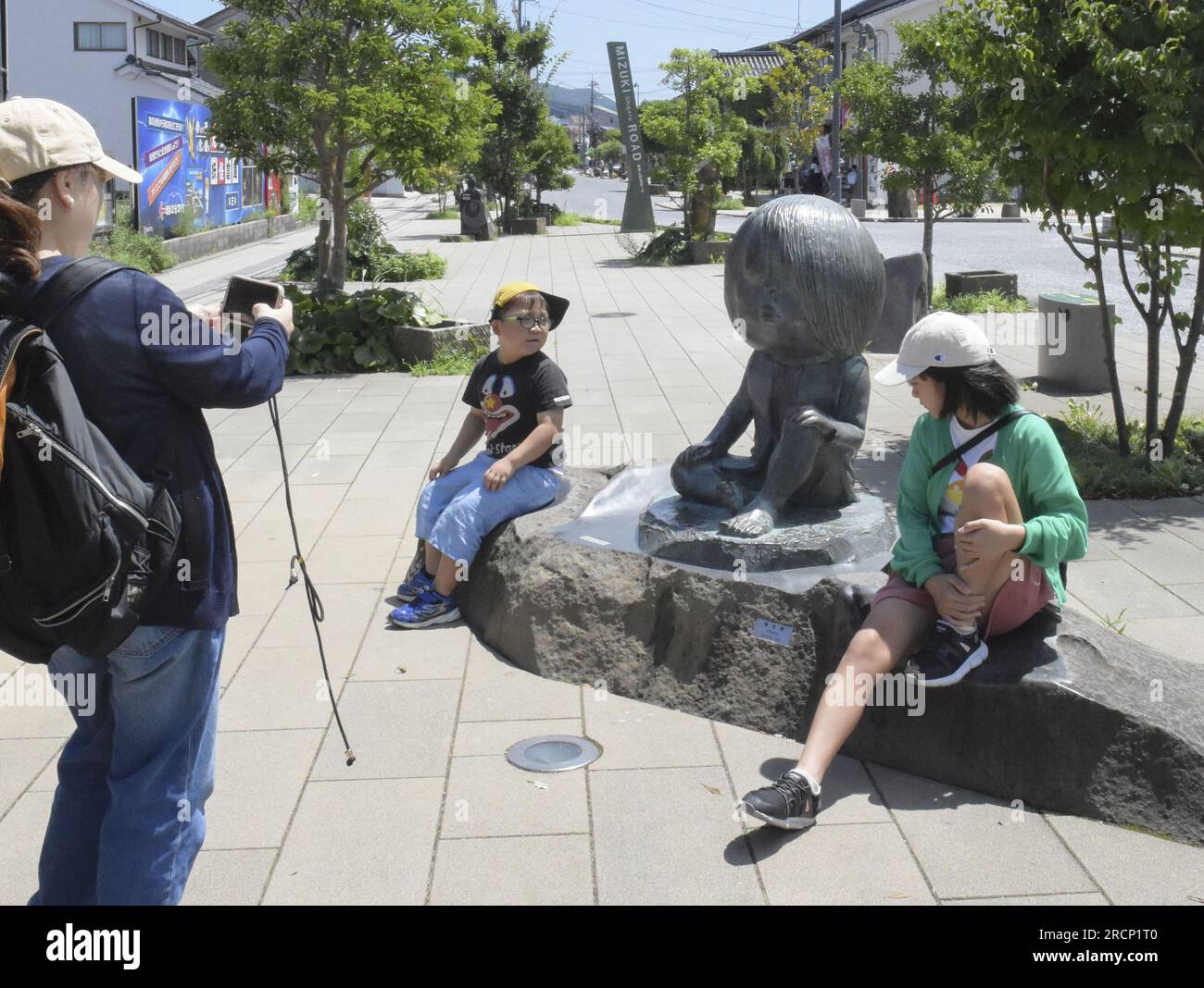 Tourists pose for a photo with a statue of a character from "Gegege no ...