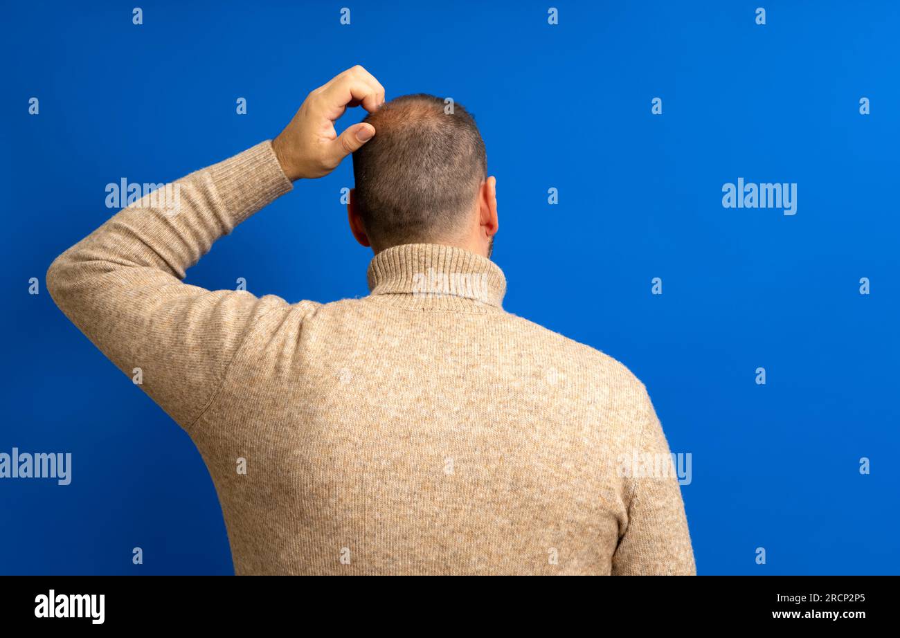 Back view of thoughtful man scratching his head over blue background ...