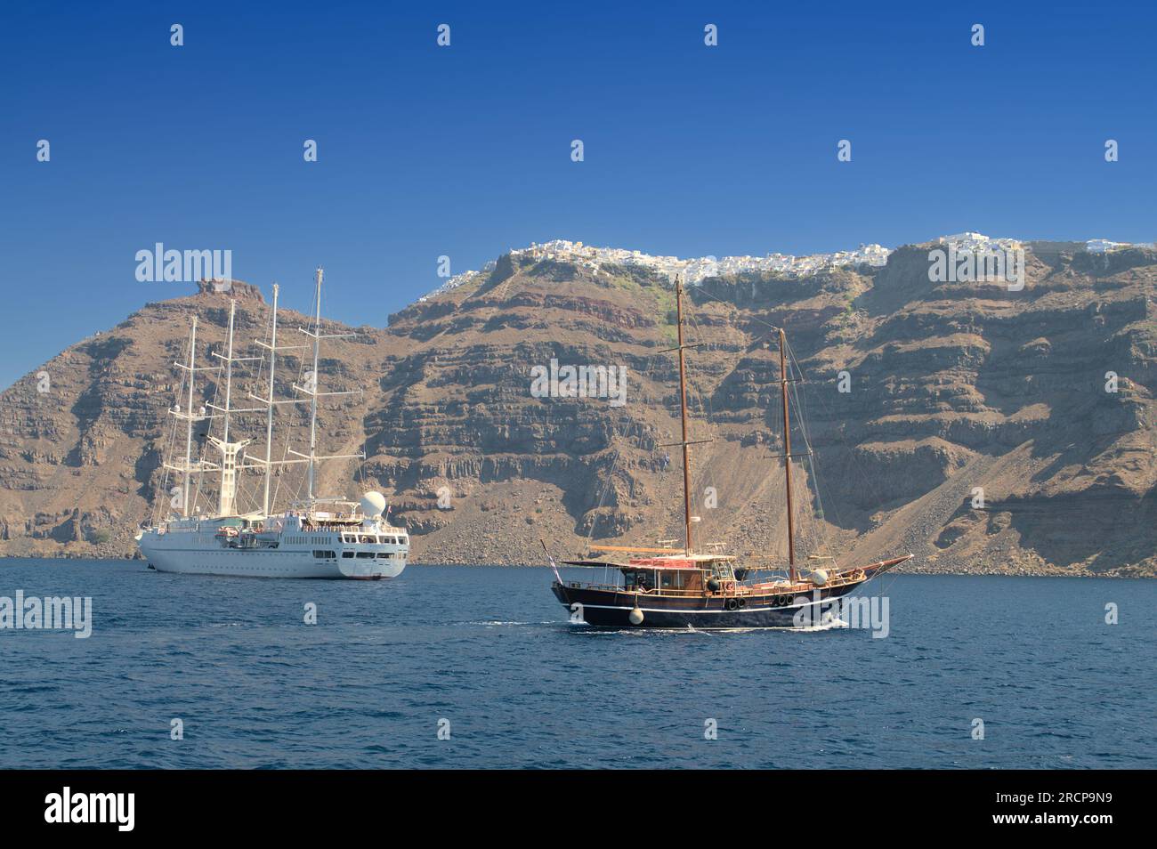 Retro schooner and modern sailing ship floating off the rocky coast of ...