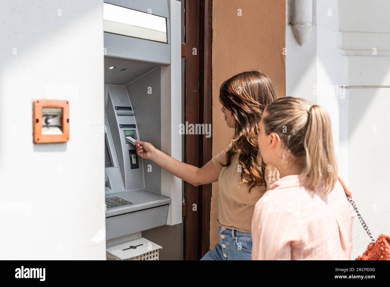 Two beautiful tourists female withdrawing the money from a bank card using ATM machine at the ...