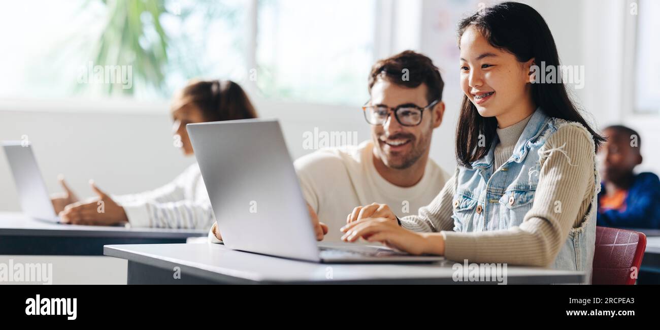 Happy young girl getting assistance from her teacher as she engages in ...