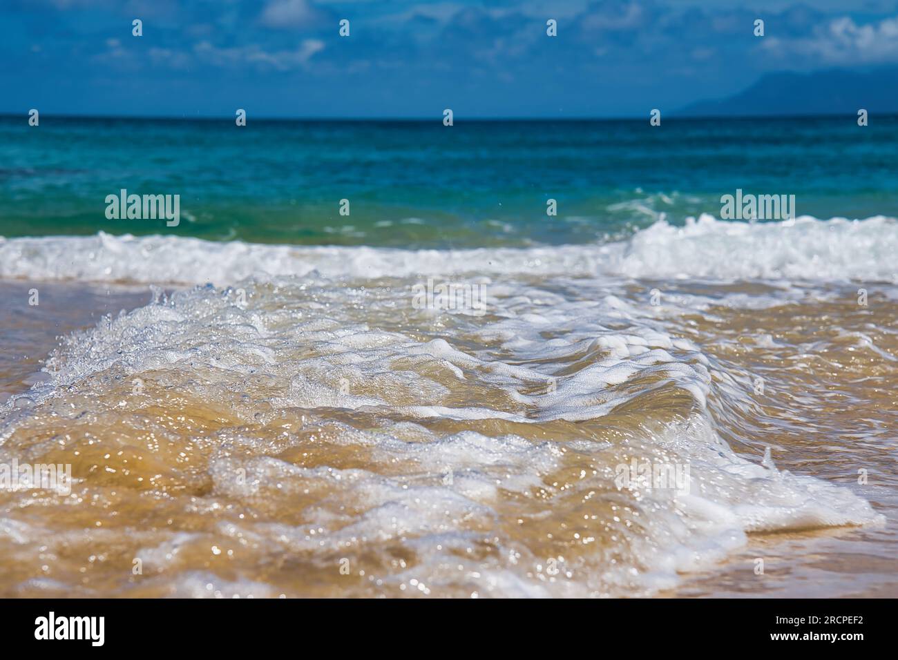 Small waves creating foam on the beach with white sand, hot day and ...