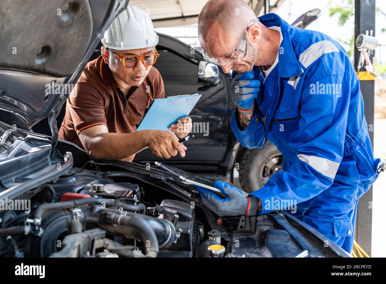 Two male auto mechanics working together on the car engine at their car ...