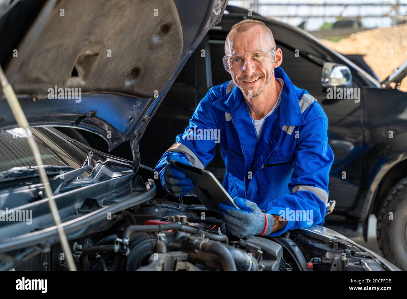 Happy car mechanic holding a computer tabet and smiling at camera while ...