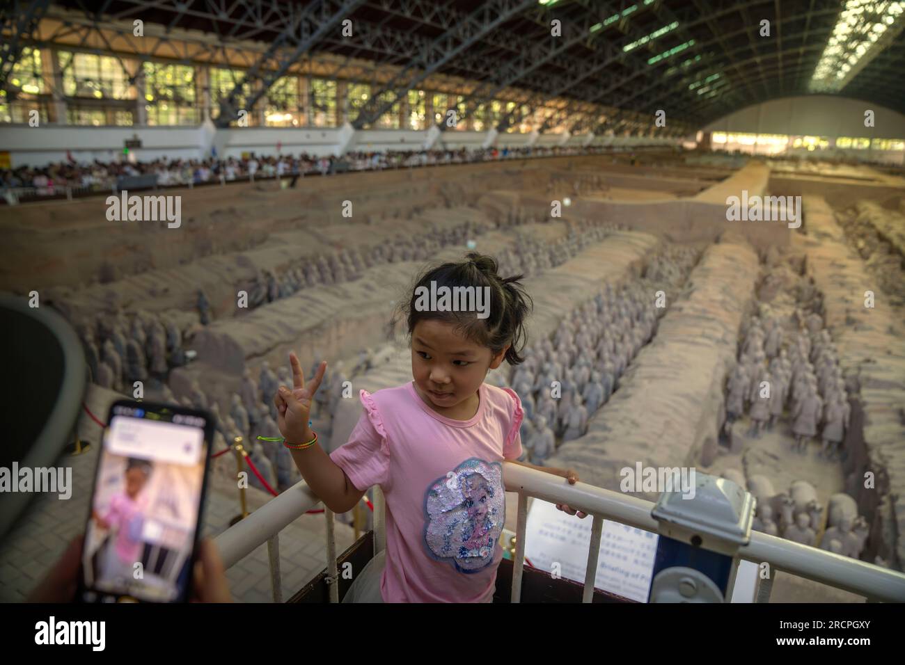 A girl poses for a photo in front of excavated figures on display at ...
