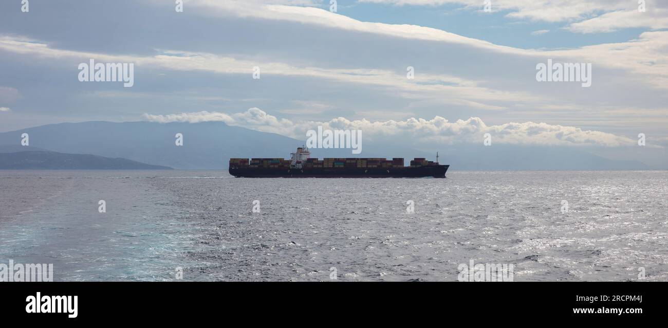 Container cargo ship full loaded is crossing the open wavy sea at dusk ...