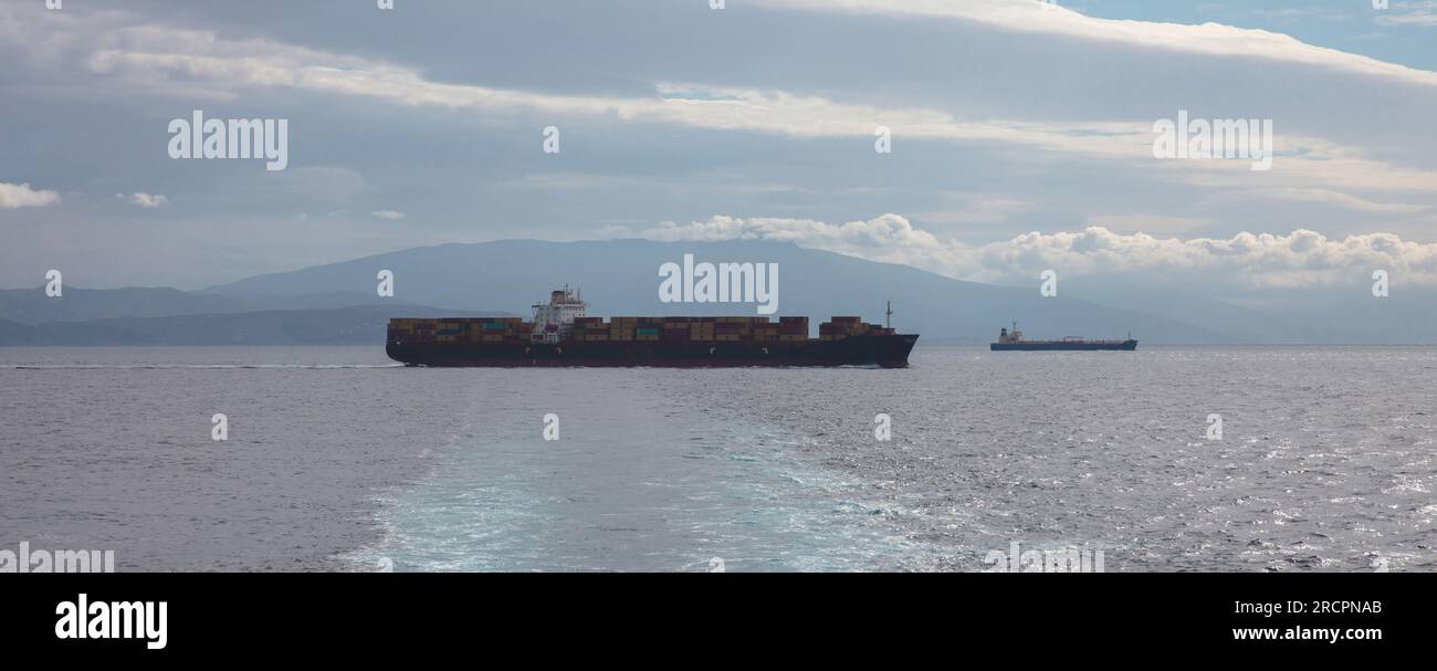 Container cargo ship full loaded is crossing the open wavy sea at dusk ...