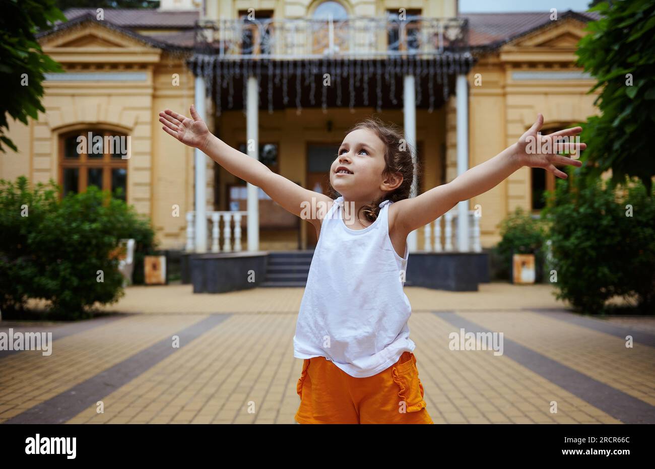 Little child girl walking in the park, smiling, raising up her arms ...