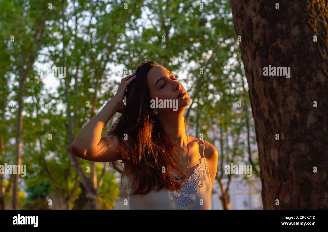 Horizontal close up shot of a pretty young woman standing beside a tree ...