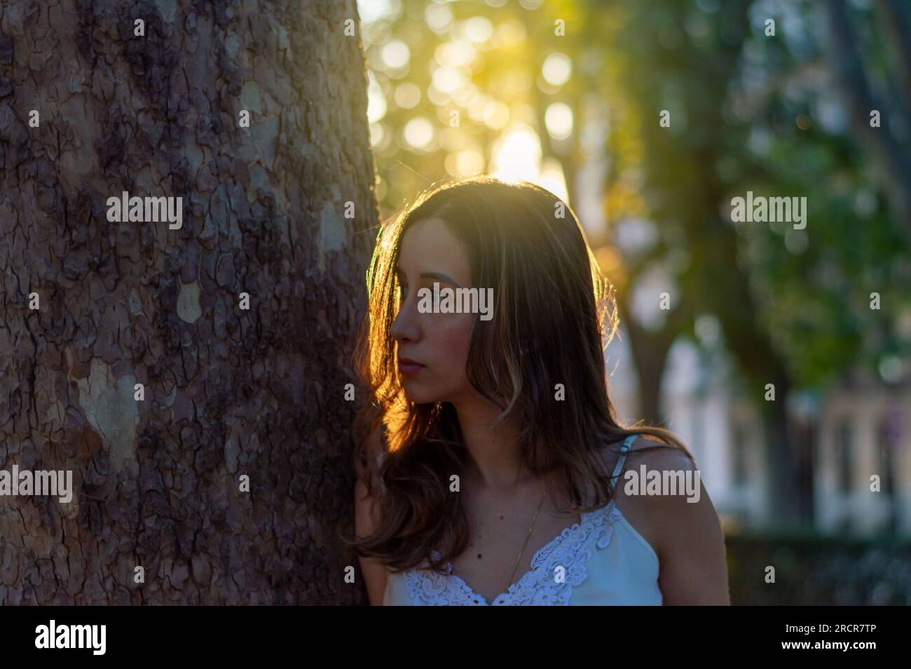 Horizontal close up shot of a pretty young woman standing beside a tree ...