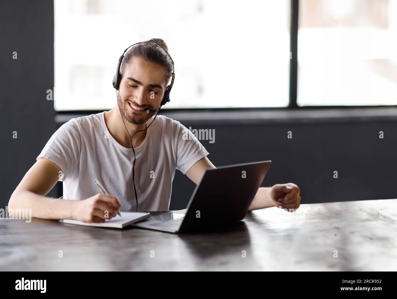 Guy Taking Notes At Laptop Posing With Headset In Office Stock Photo ...