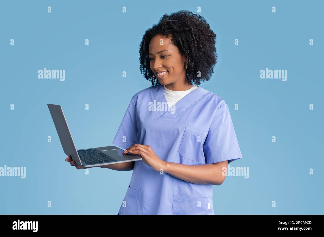 Glad young black lady doctor nurse in blue uniform uses laptop for ...