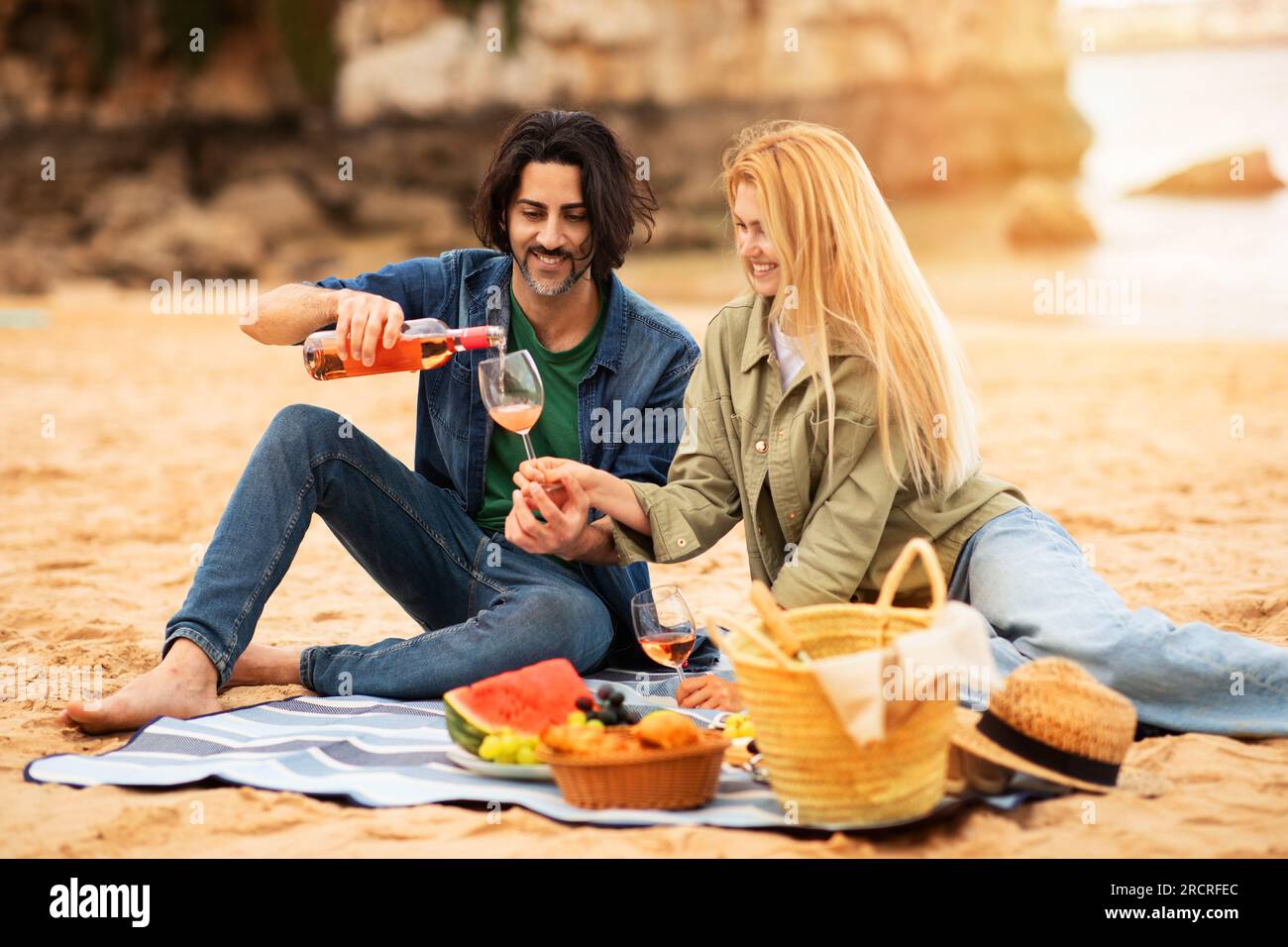 Young Man And Woman Having Picnic On Beach Near Sea, Pouring Wine Stock ...