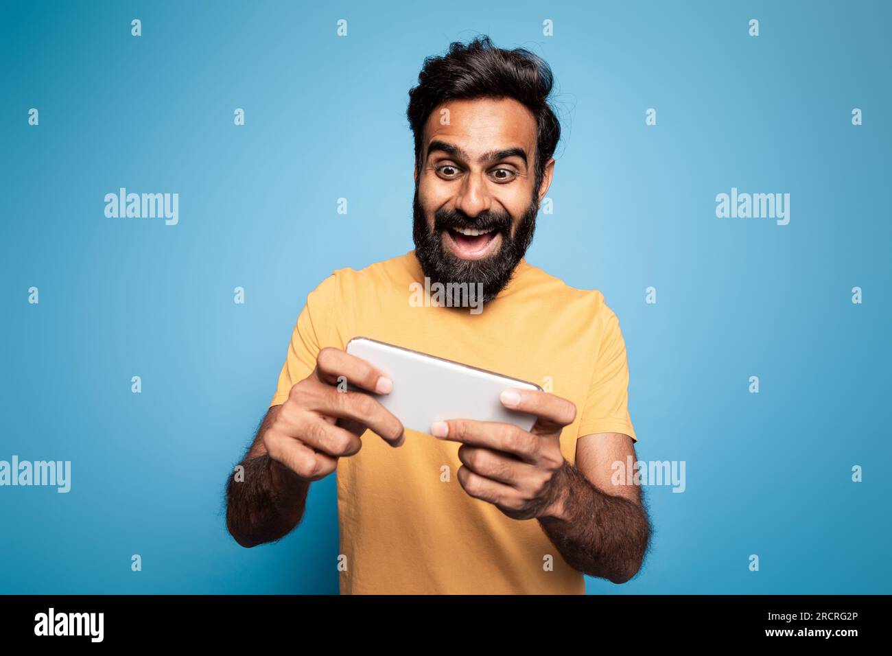 Gadget addiction concept. Happy middle aged indian man playing mobile ... Gadget addiction concept. Happy middle aged indian man playing mobile ...