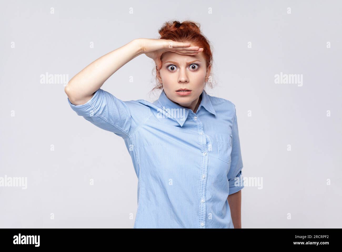 Portrait of scared ginger woman wearing blue shirt keeping palm over ...