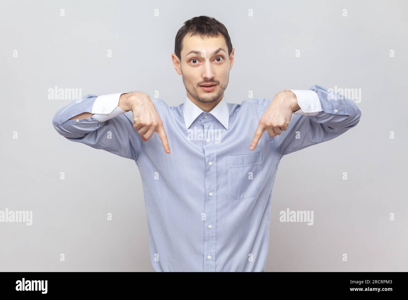 Portrait of serious strict young adult man standing pointing both index ...