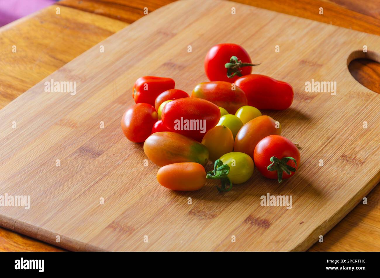 Multi coloured tomatoes sitting on a natural wood table with chopping ...