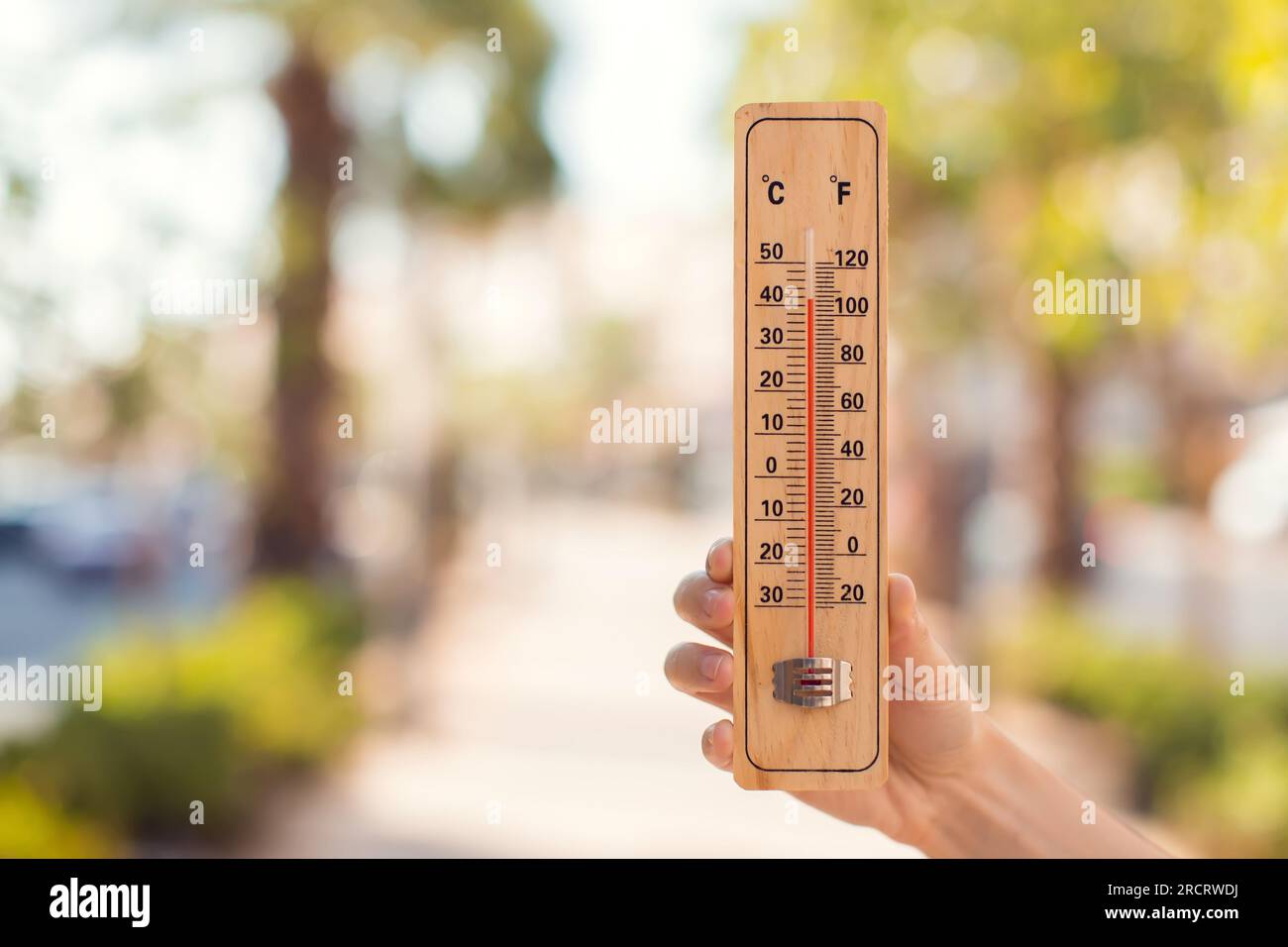 Hot weather. Thermometer in hand in front of street with trees and ...