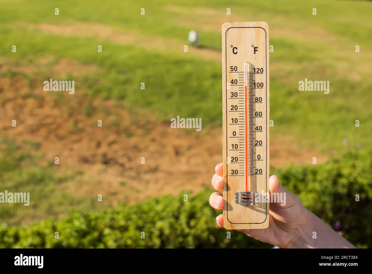 Hot weather. Thermometer in hand in front of dry grass during heatwave ...
