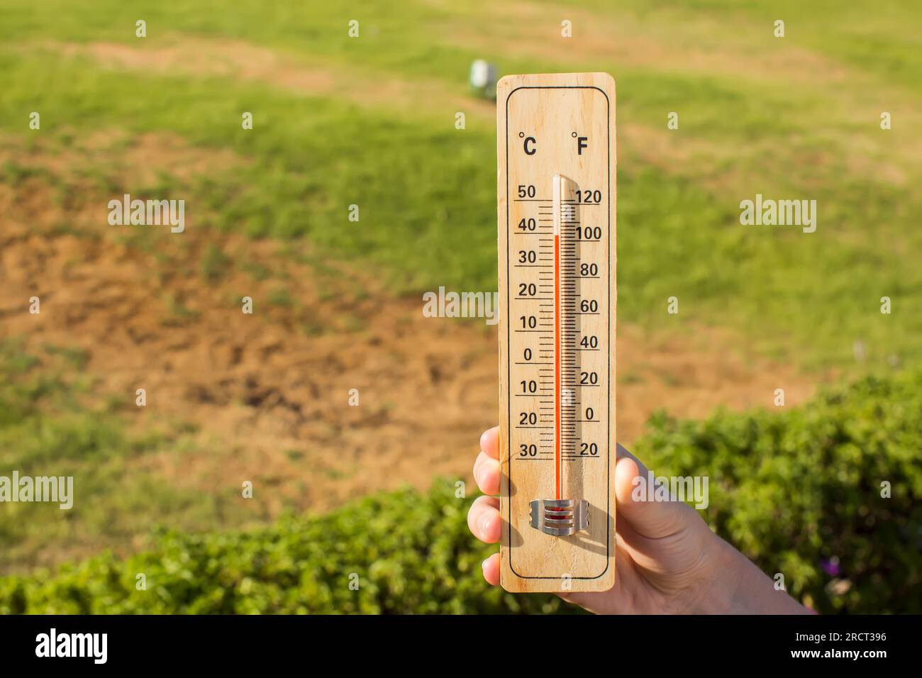 Hot weather. Thermometer in hand in front of dry grass during heatwave ...