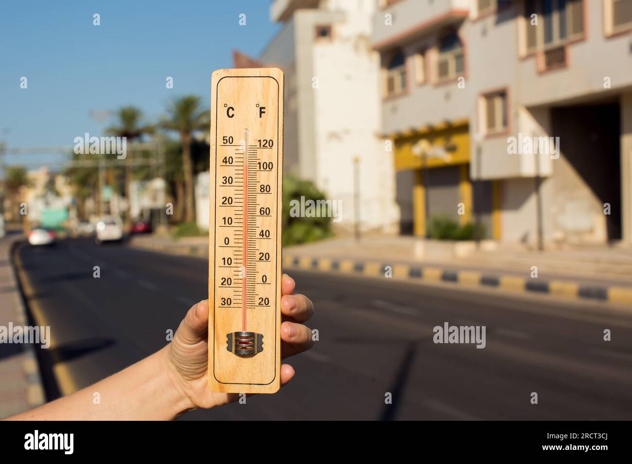 Hot weather. Thermometer in hand in front of an urban scene during ...