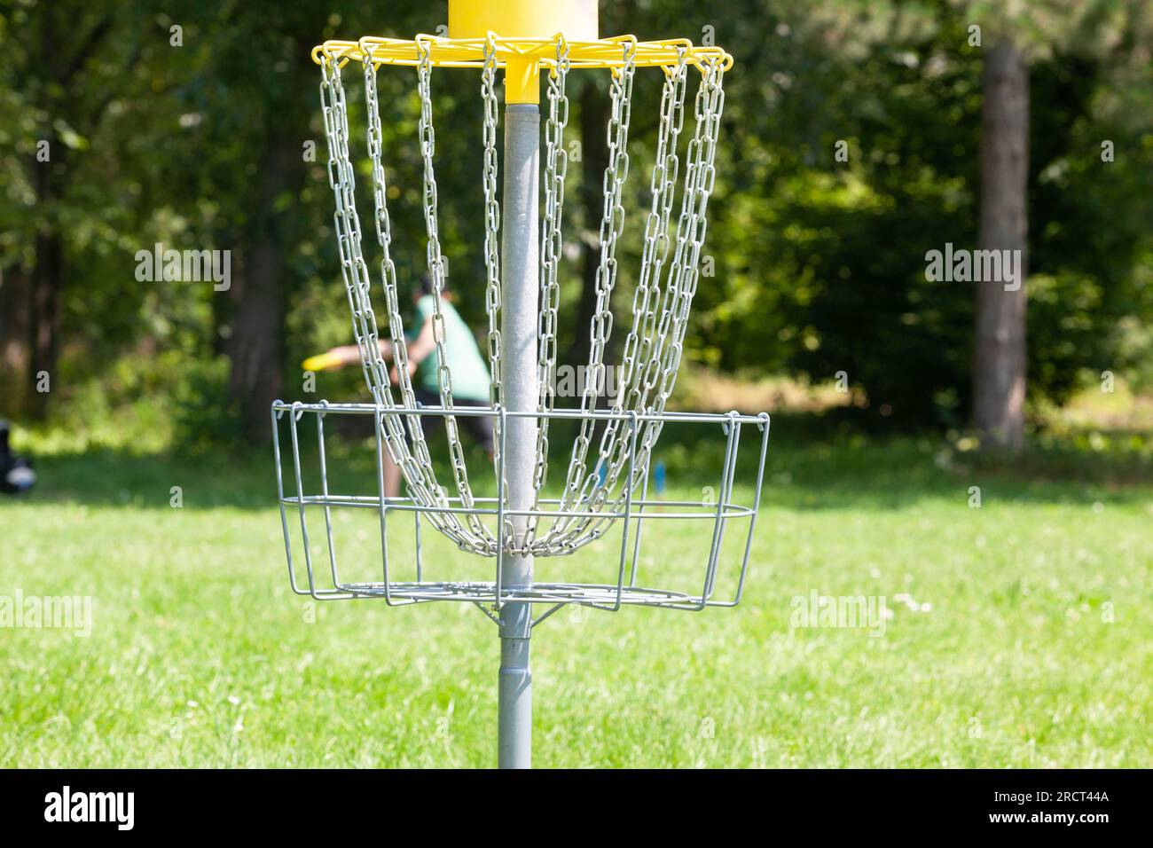 Disc golf player throwing a flying disc in the park, chain basket in ...