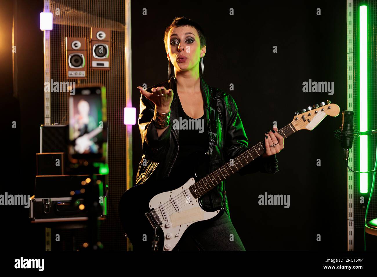 Rockstar blowing air kisses in front of smartphone camera while playing at electric guitar in ...