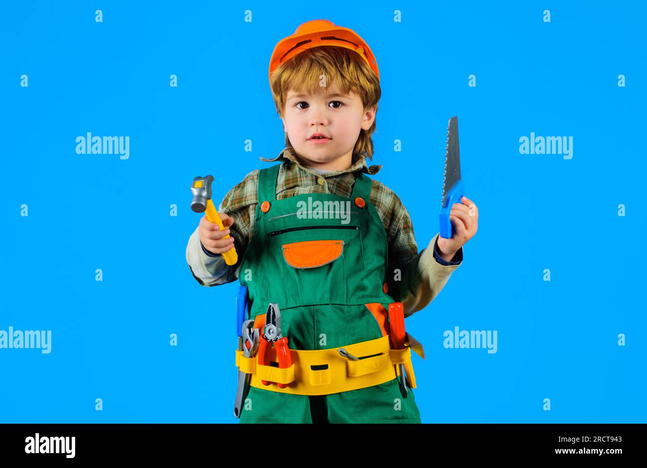 Little builder kid in safety helmet with saw and hammer. Little ...