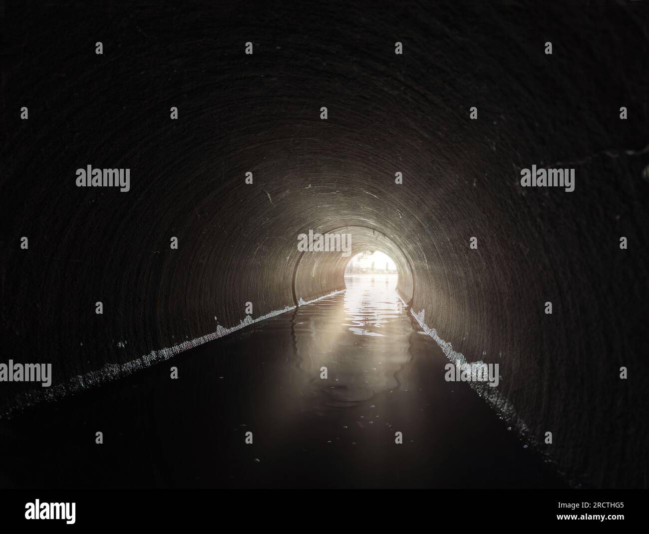 Light at end of round flooded sewer tunnel. Exit from sewer system ...