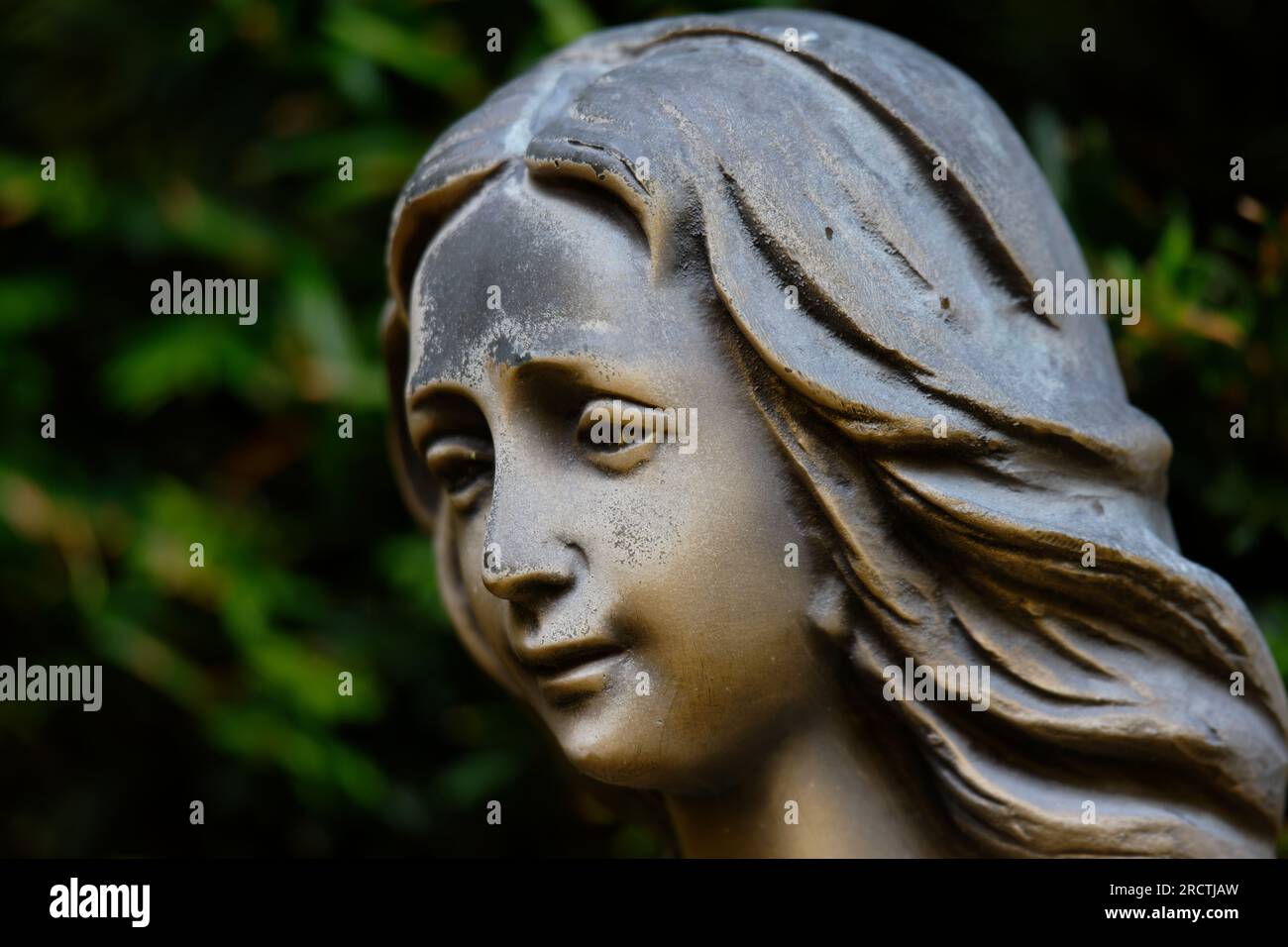 portrait of sad looking female cemetery statue against blurred green ...