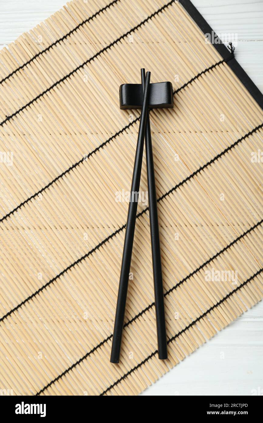 Bamboo mat with pair of black chopsticks and rest on white table, top ...