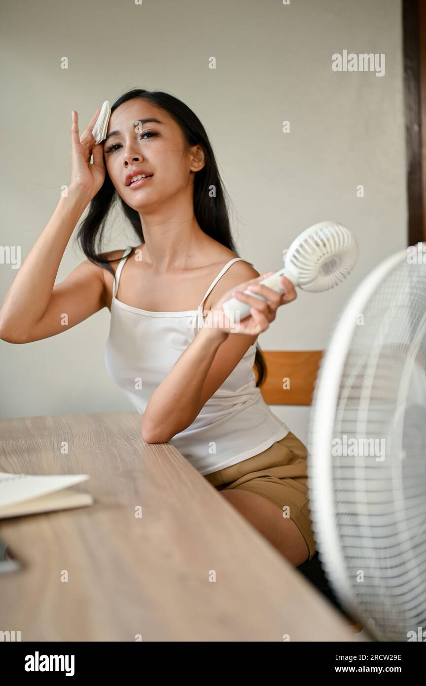 A portrait of a beautiful Asian woman feeling overheated, suffering ...