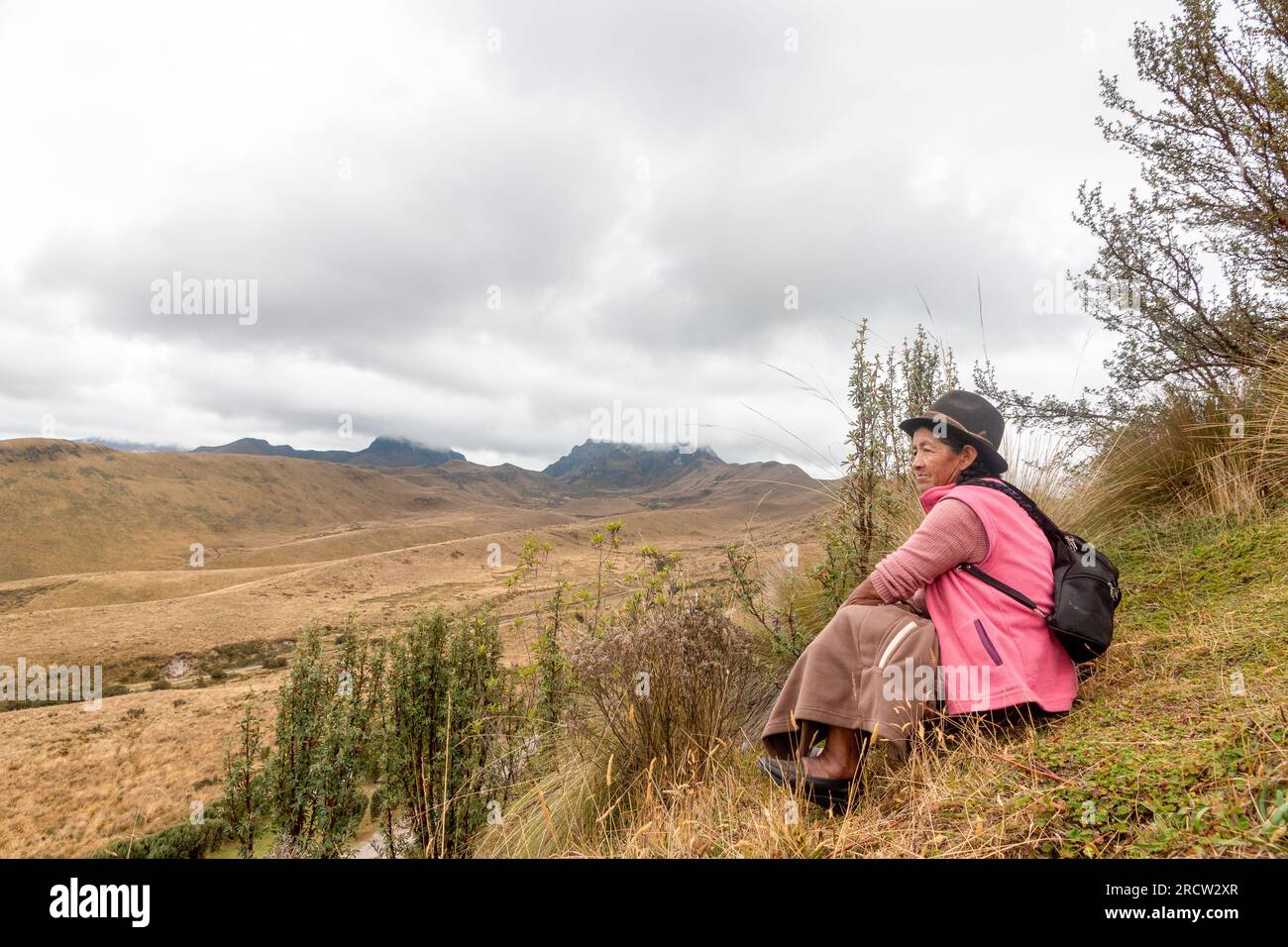 A lone indigenous woman sitting on a hilltop looks out over the wild ...