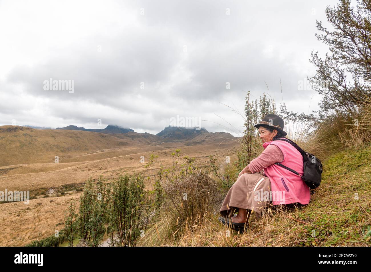 A lone indigenous woman sitting on a hilltop looks out over the wild ...