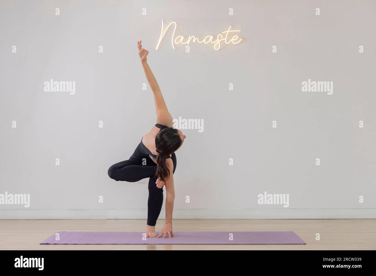 Woman practicing yoga in a studio makes a standing pose, with a namaste ...
