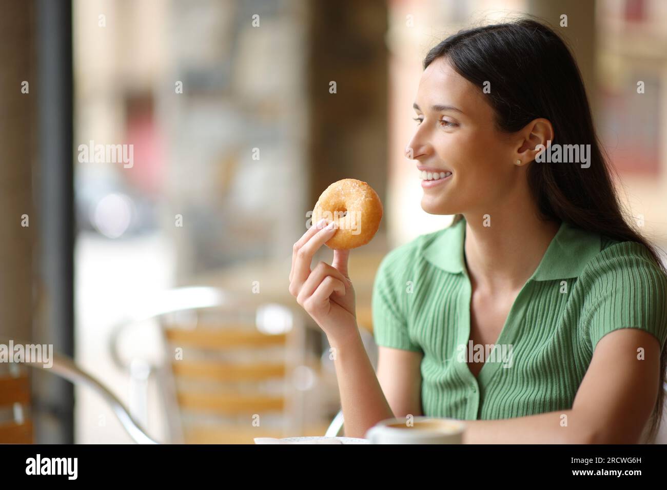 Happy woman eating doughnut sitting in a coffee shop terrace Stock ...
