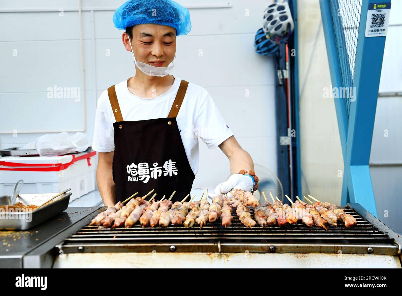 QINGDAO, CHINA - JULY 16, 2023 - A stall owner grills meat kebabs at ...