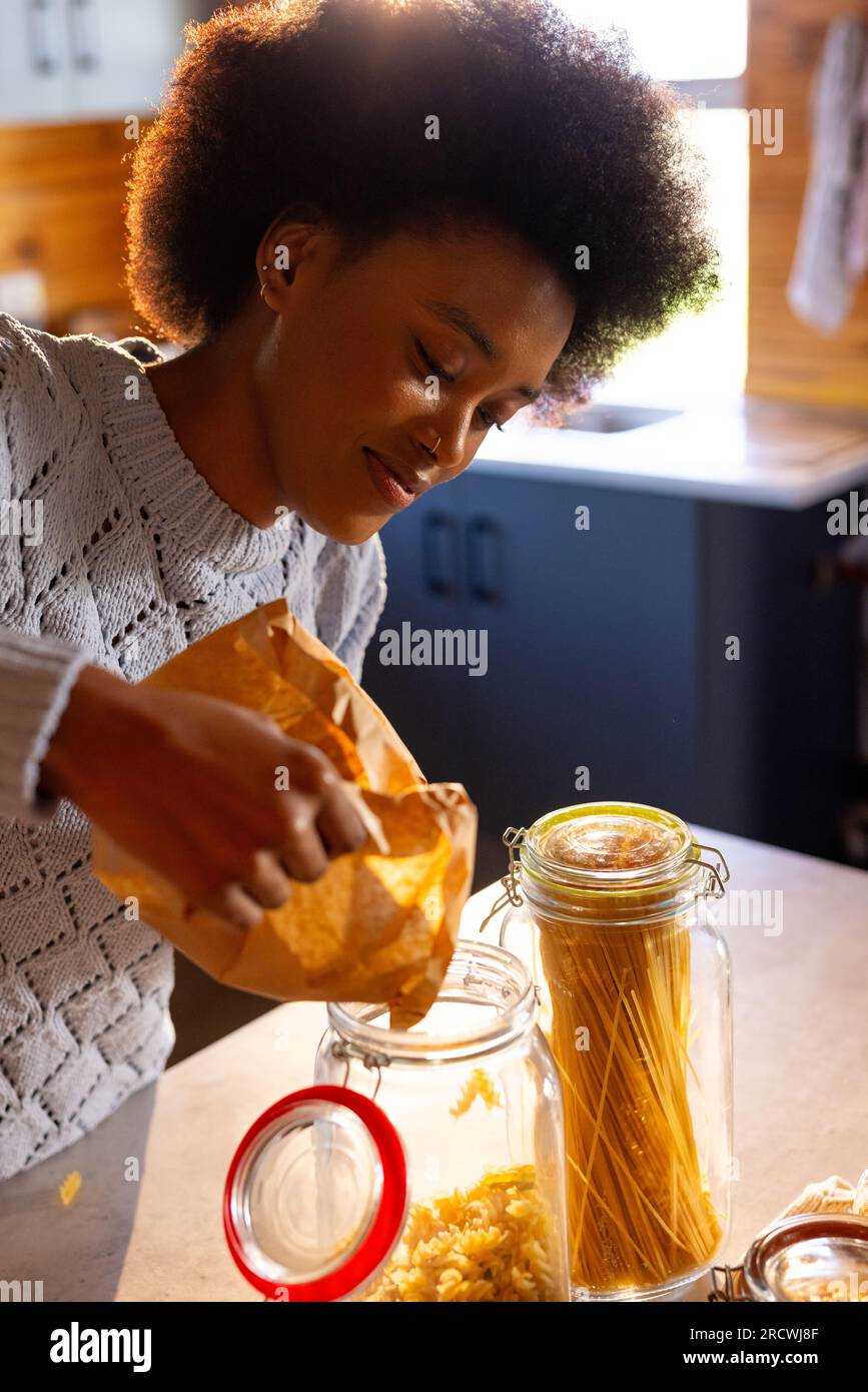 Happy african american woman pouring pasta from paper bag to storage ...
