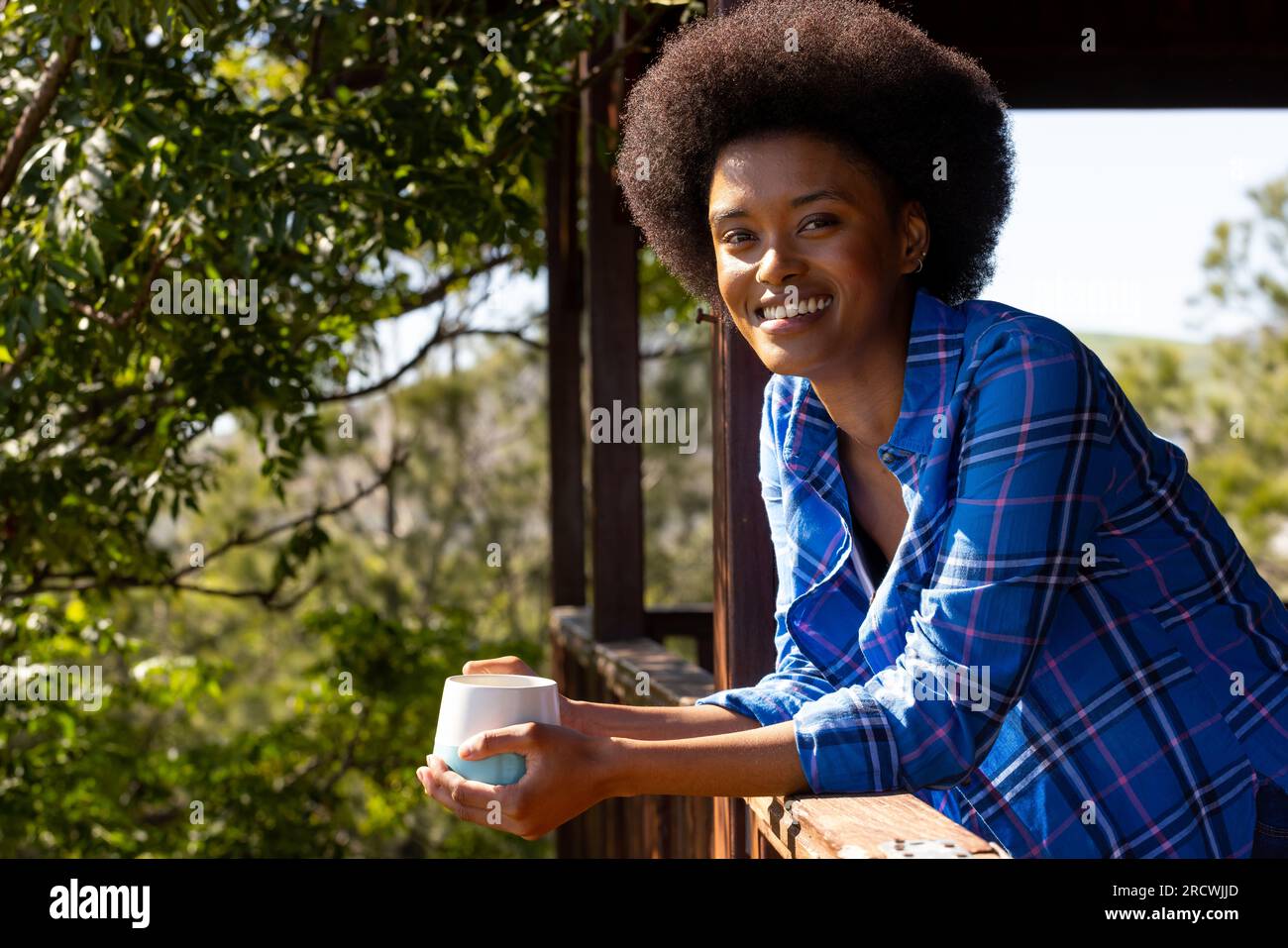 Happy african american woman leaning on balcony with cup of tea ...