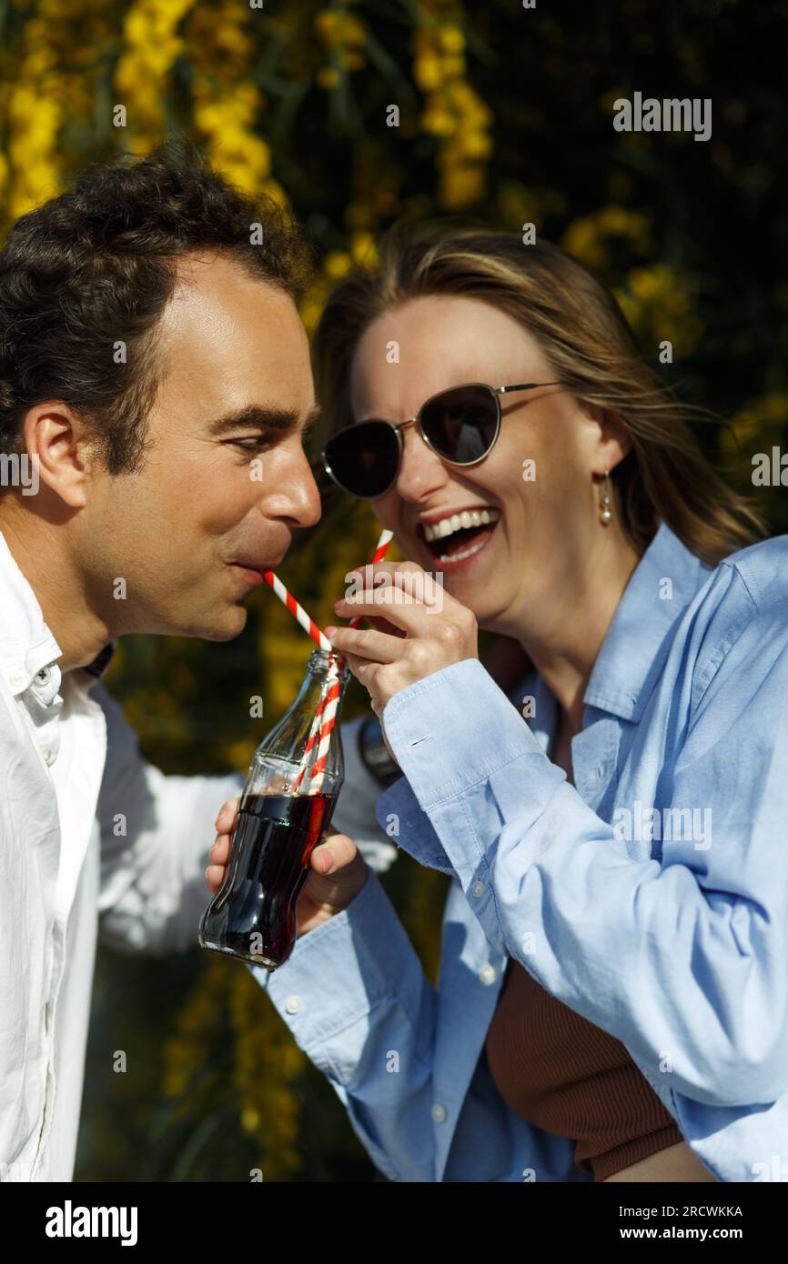 Young happy couple outdoors drinking cold drink from glass bottle with ...
