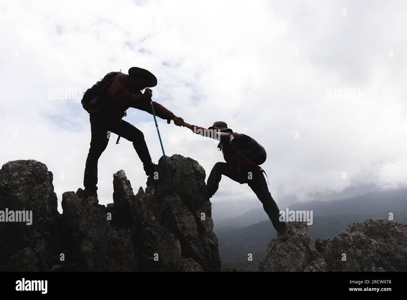 Silhouette of Two male hikers climbing up mountain cliff and one of ...