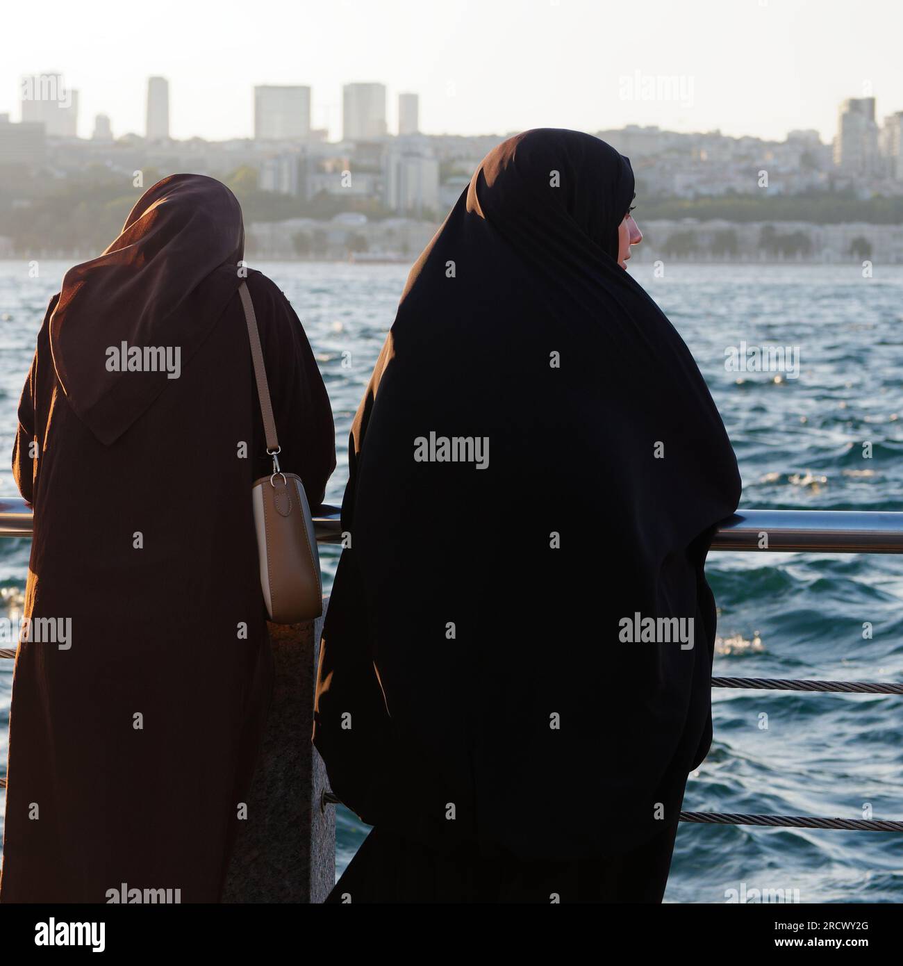 Two Muslim woman enjoy the summer sun setting over the Bosporus Sea ...