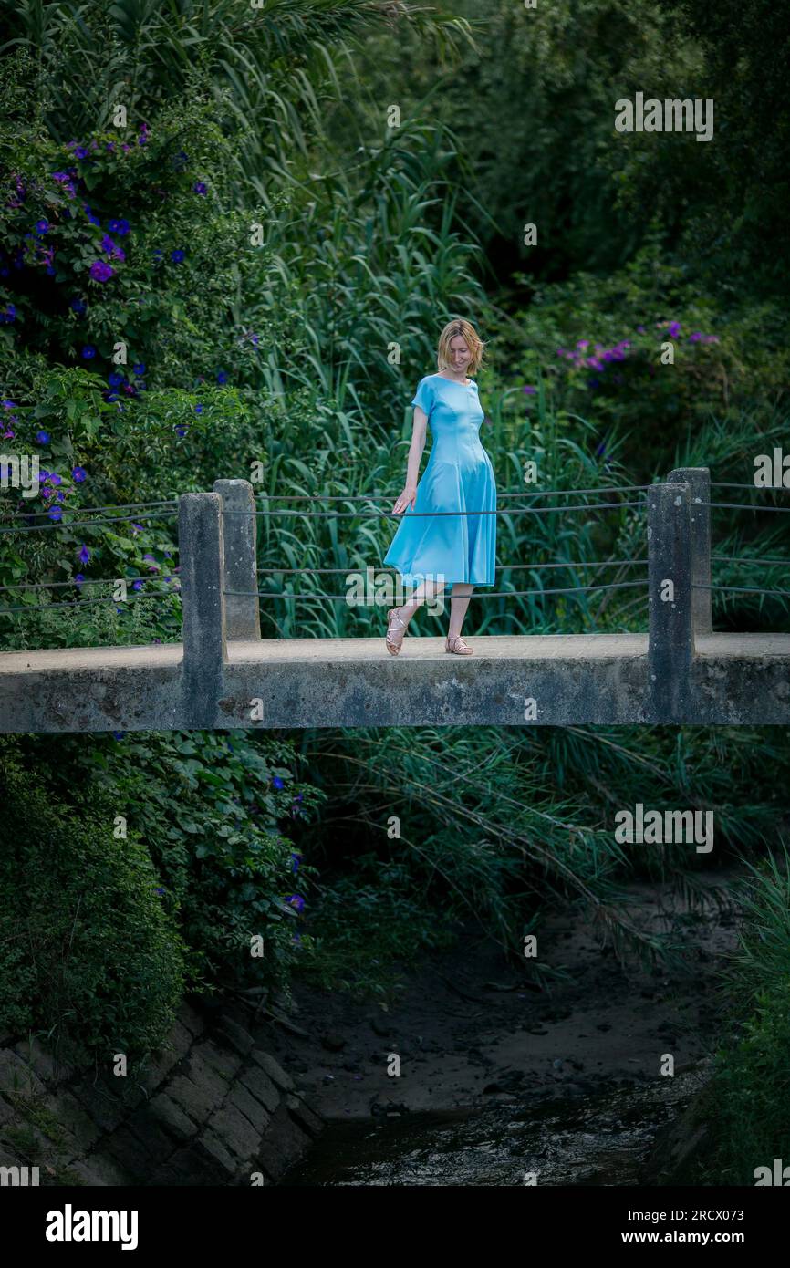 A woman wearing a blue dress stands on an ancient suspended bridge ...