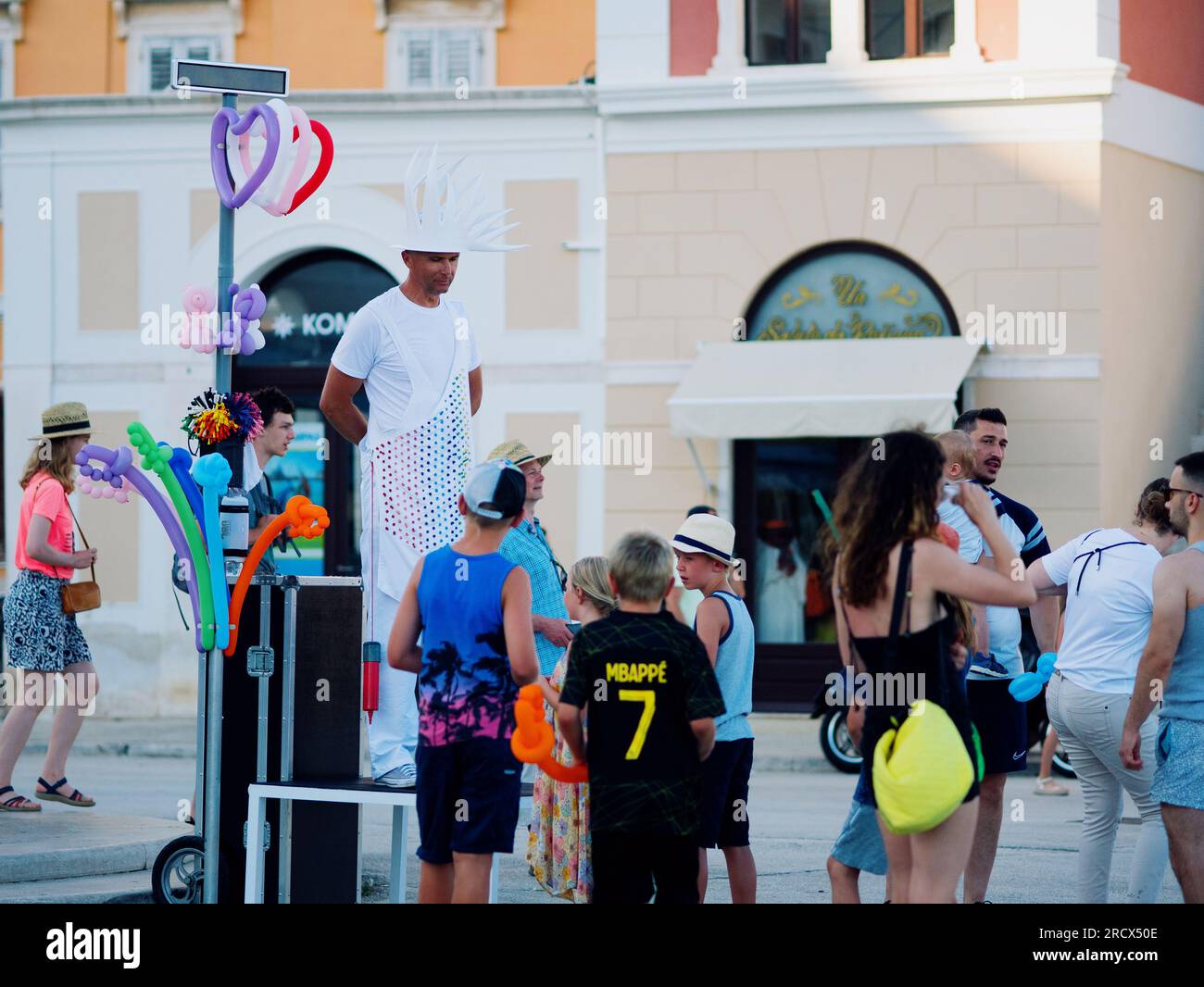 Street performer in white suit and fabulous hat makes inflatable toys ...