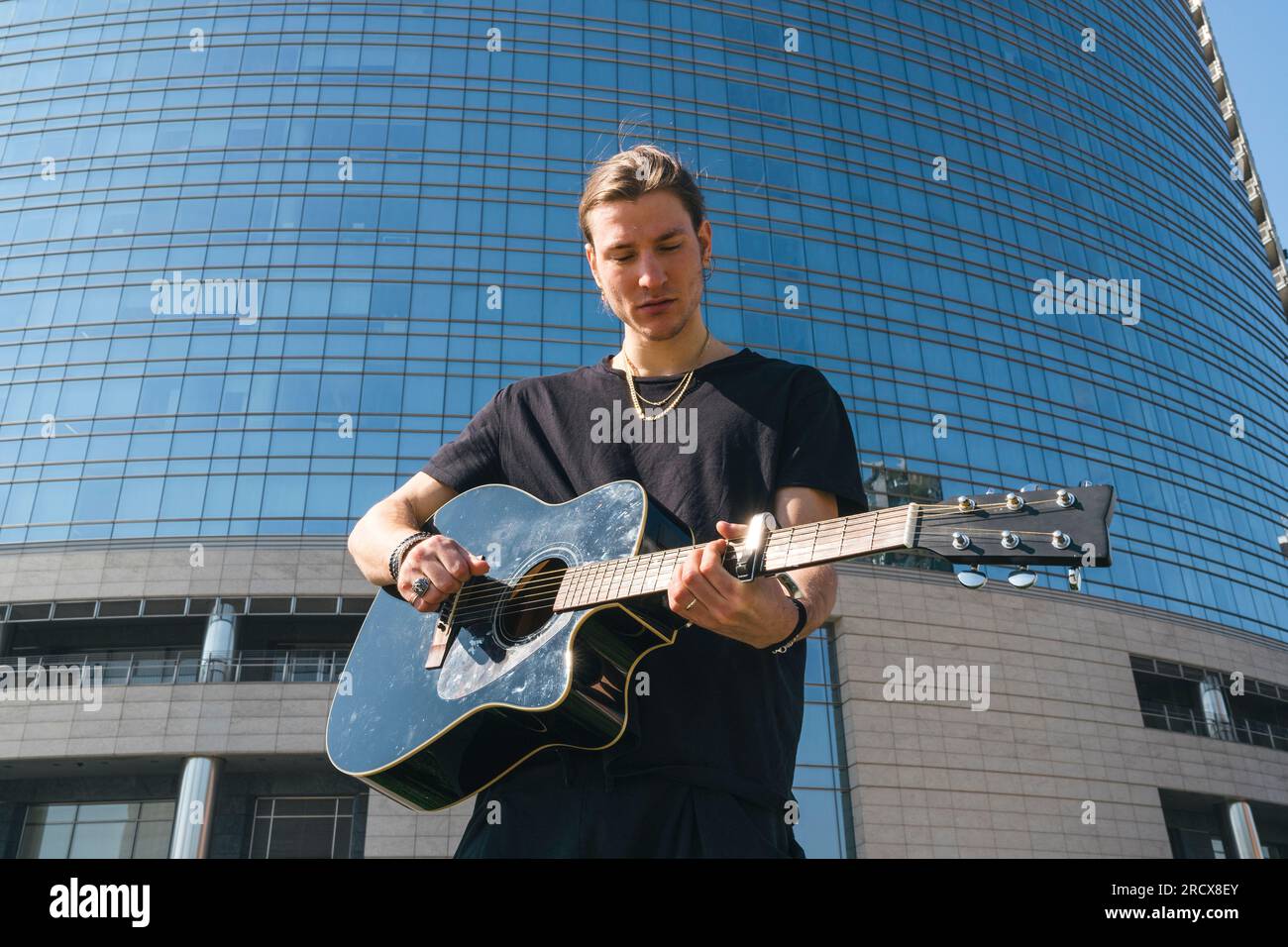 white man stand in front of a sky screaper is playing a classic guitar ...